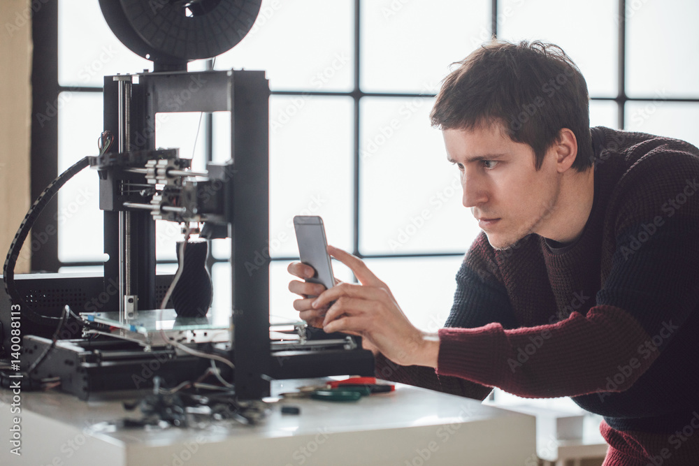 Young Caucasain man graphic designer taking photo of 3d printing ...