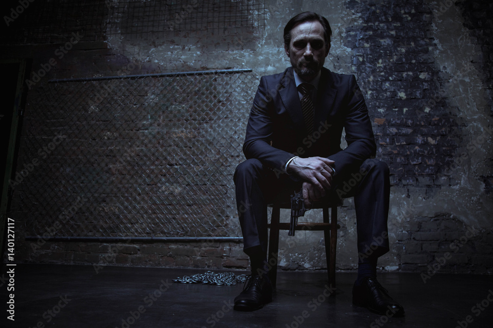 Charming villain sitting in dark room Stock Photo | Adobe Stock