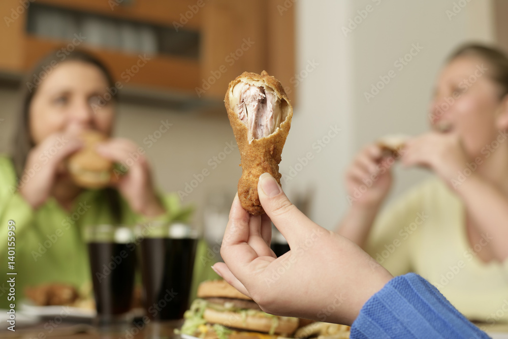Female hand holding up a chicken wing in front of two women, selective ...