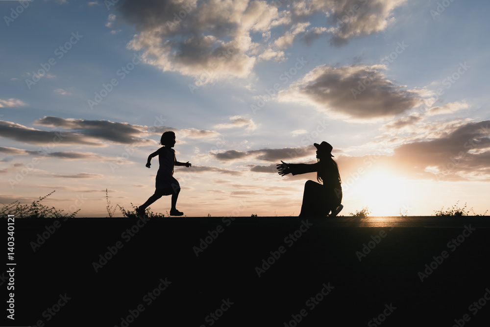 a silhouette of a happy girl child running into the arms of his loving ...
