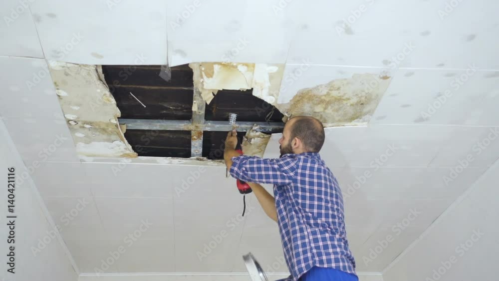 Man repairing collapsed ceiling. Ceiling panels damaged huge hole in ...