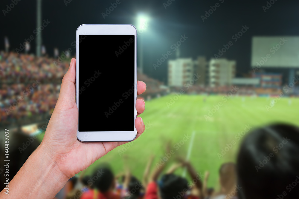 Hand holding smartphone with soccer screen in football stadium ...