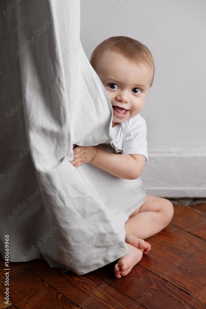 cute baby hiding himself behind the living room curtain and smiling ...
