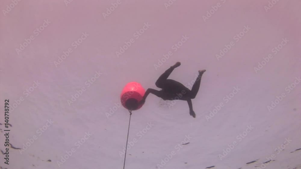 Underwater model free diver swims with red buoy in clean blue water in ...