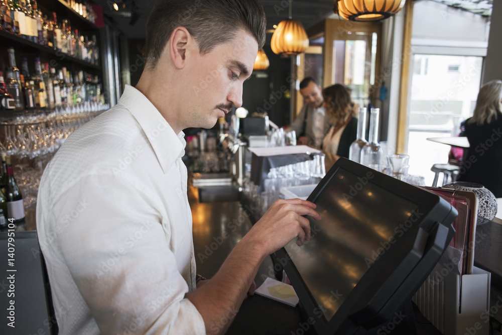 Side view of male owner using cash register at checkout in restaurant ...
