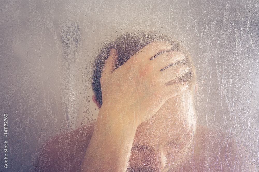 stressed man taking a shower standing under flowing water and holding ...