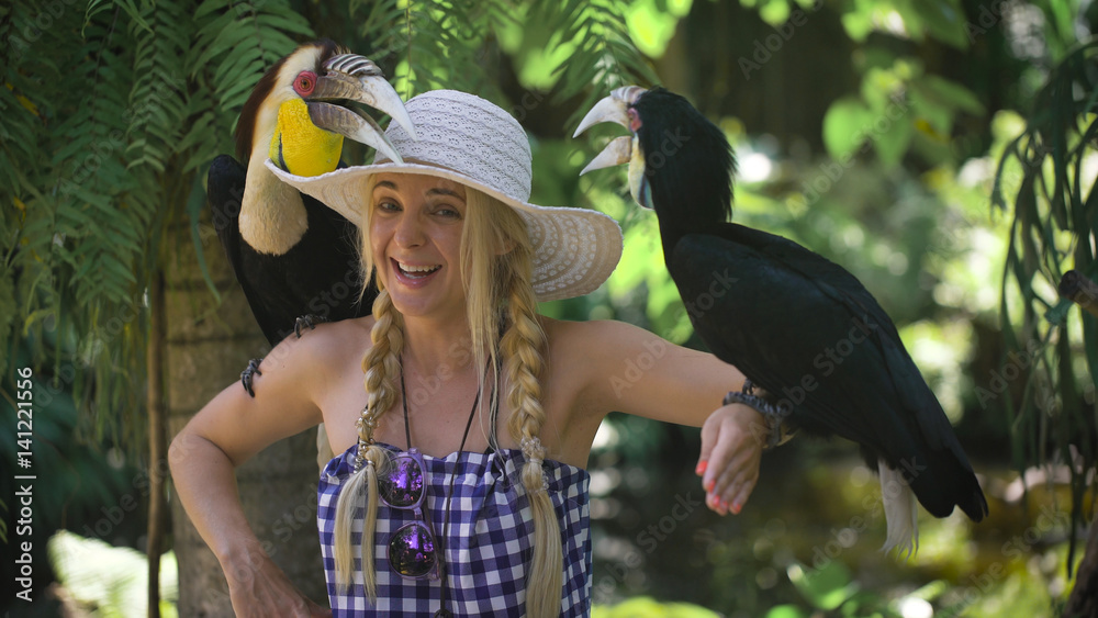 Happy fair-haired girl standing in tropical park with two big black-and ...