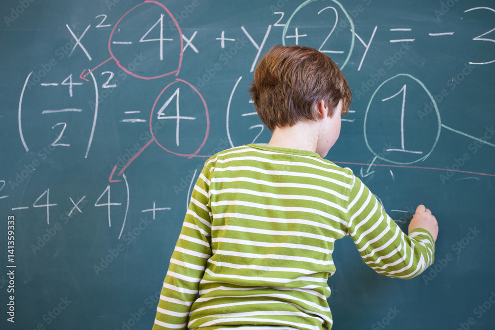 Rear view of primary schoolboy answering equation on classroom ...