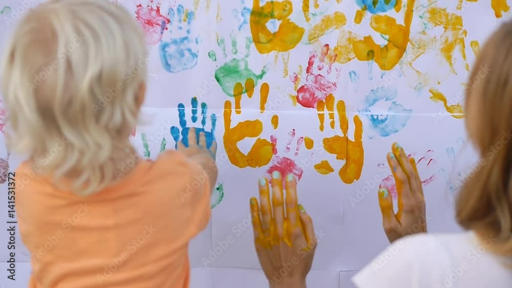 Cute little child painting color handprints on the white wall with ...