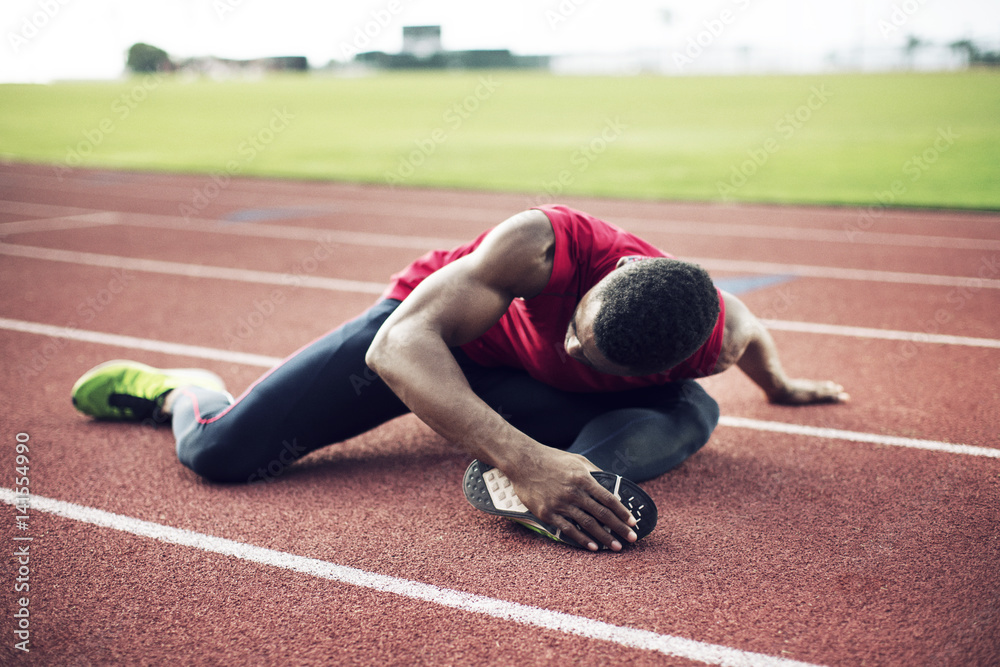 Sportsman sitting on running track and stretching Stock Photo | Adobe Stock