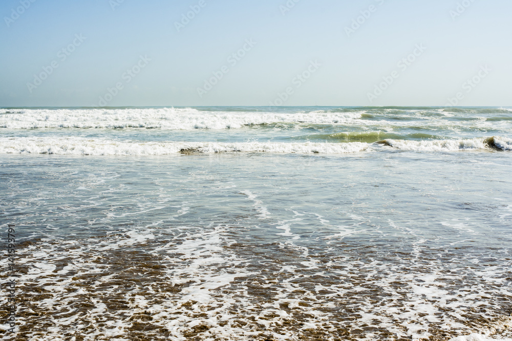 Sea tidal waves with white foam on a sunny sandy beach in resort on ...