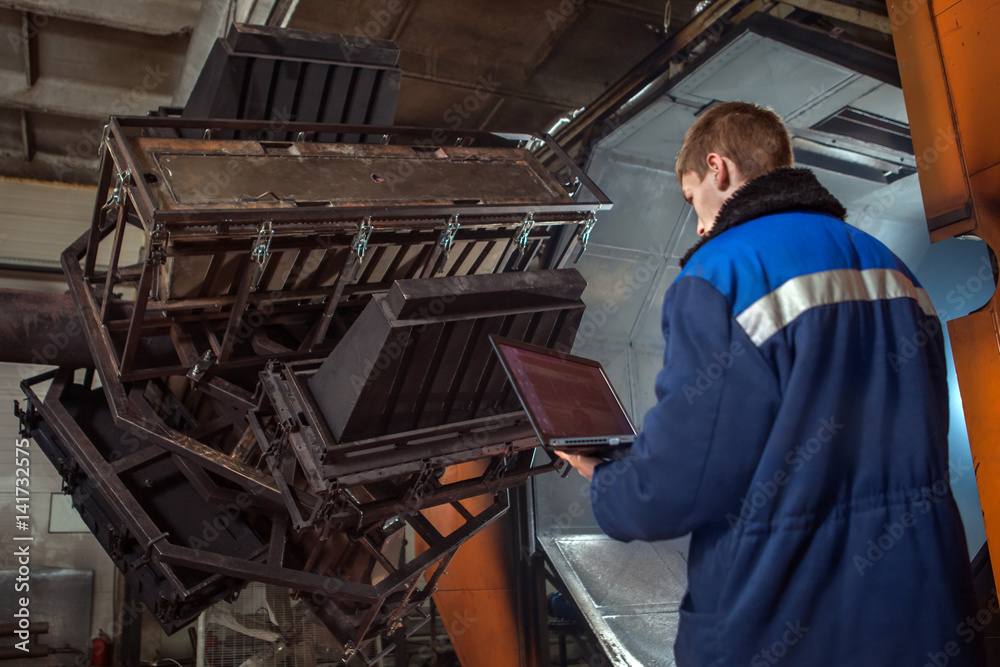 Molding plastics in the huge factory oven. Worker with the laptop is ...