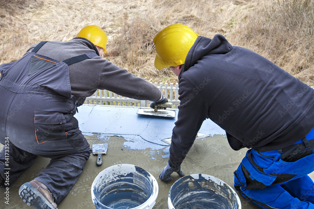 Industrial worker on construction site laying sealant for waterproofing ...