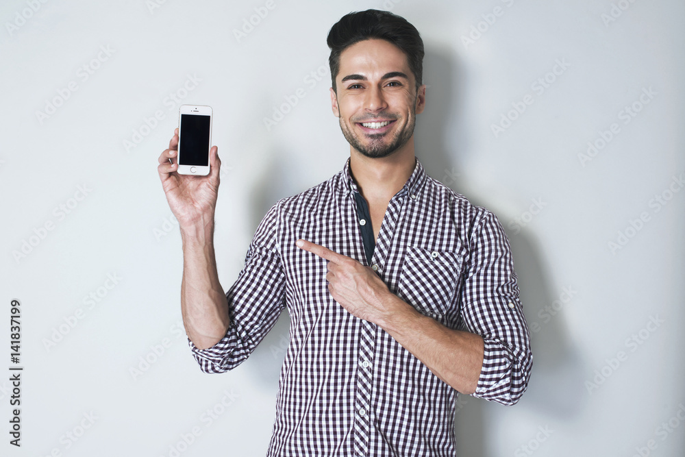 Look at the screen. Attractive young man holding his smartphone and ...