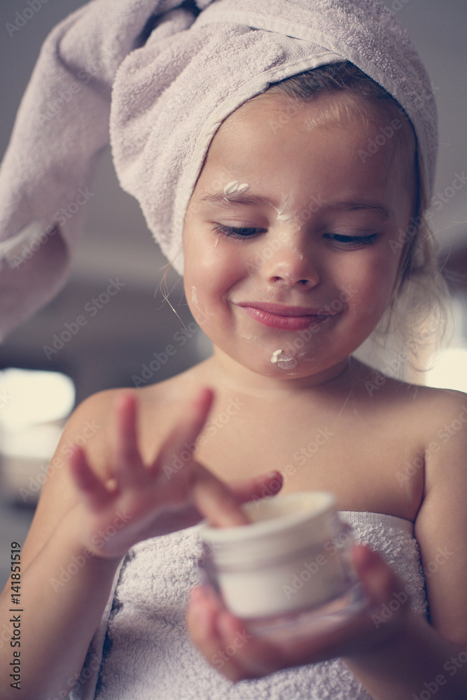 Little girl putting cream on her face. foto de Stock | Adobe Stock