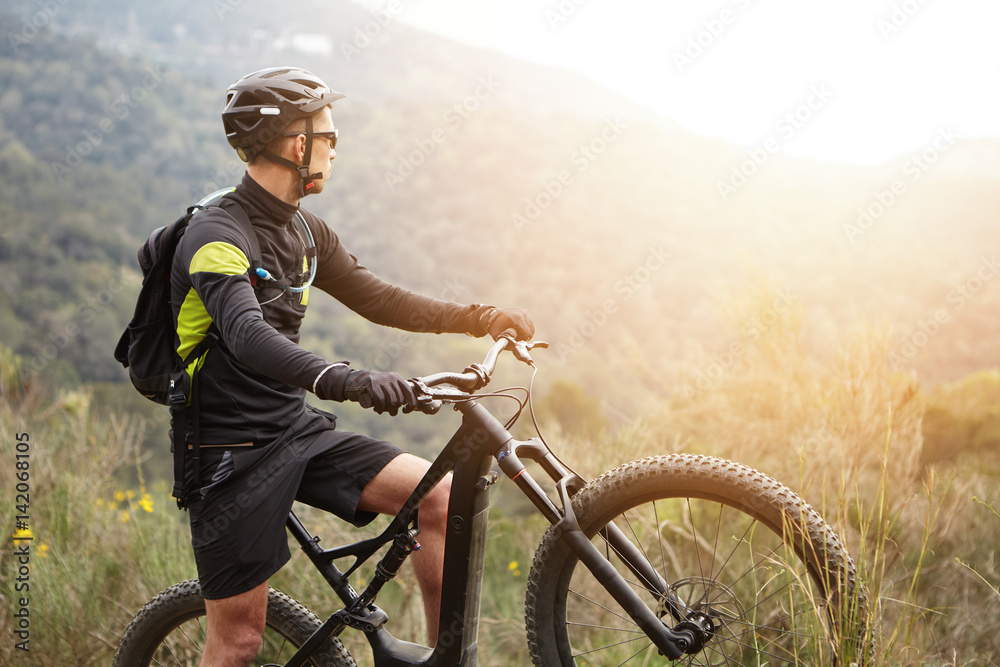 Side view of young stylish male biker in black sportswear standing on ...