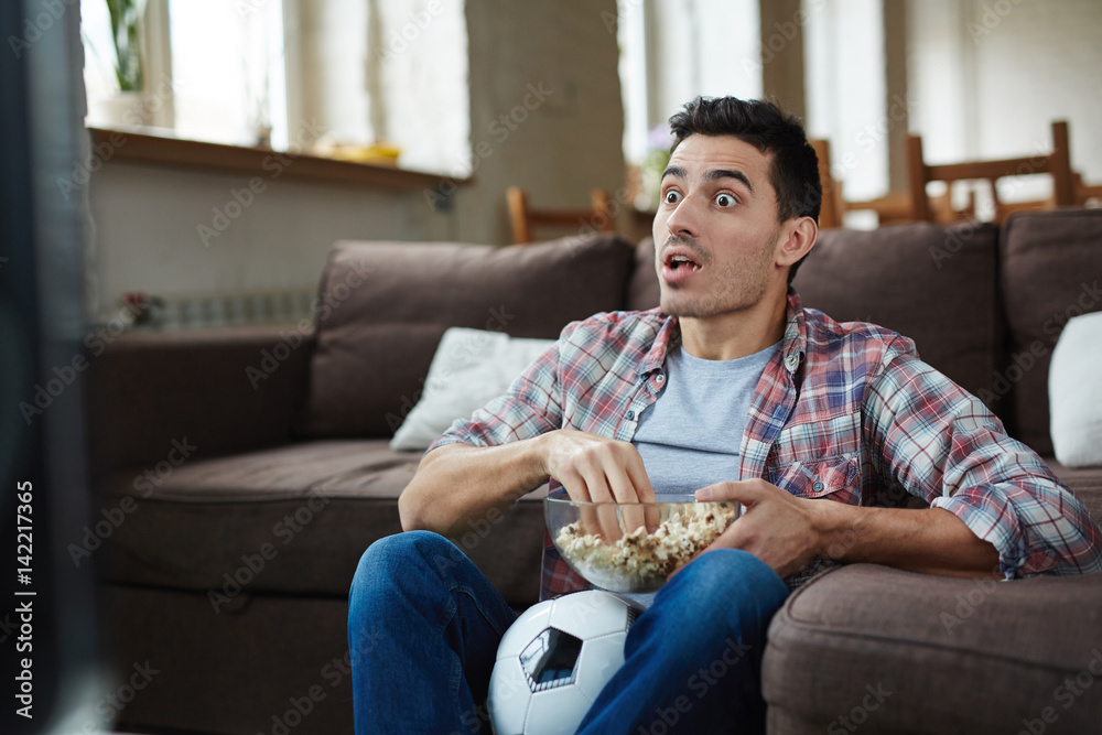 Portrait of emotional man watching football match on TV and eating ...