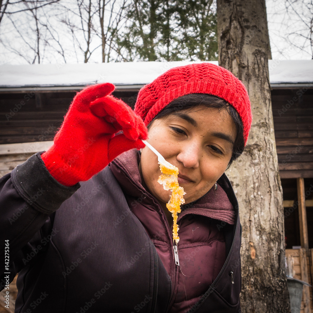 young smiling woman getting ready to eat warm maple syrup on snow, a ...