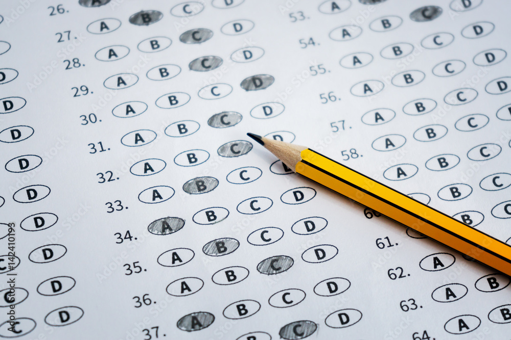 A pencil sitting on a test bubble sheet and alarm clock, optical form ...