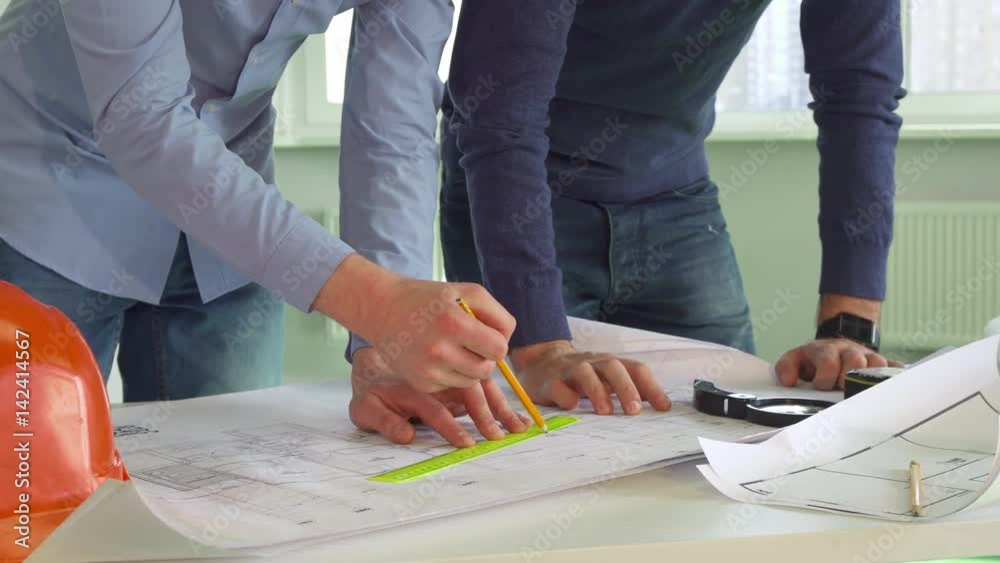 Two young architects making marks on the plans of the building. Close ...