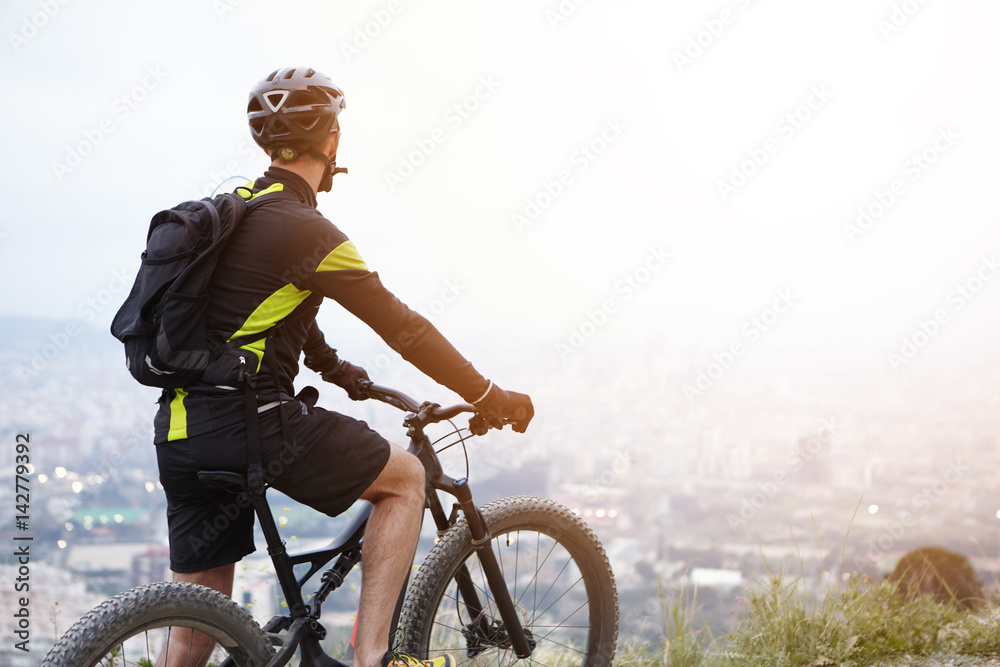 Rear shot of young rider standing on top of hill with booster bike and ...