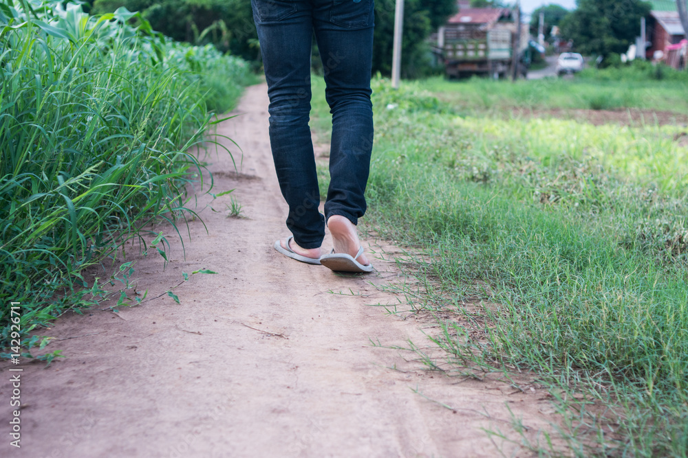 Close up young adult man walking away on path through the grass field ...