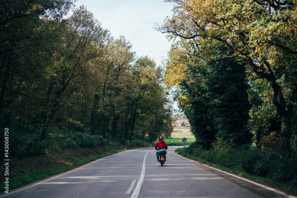 Motorcycle rider on the open and empty forest road surrounded by autumn ...