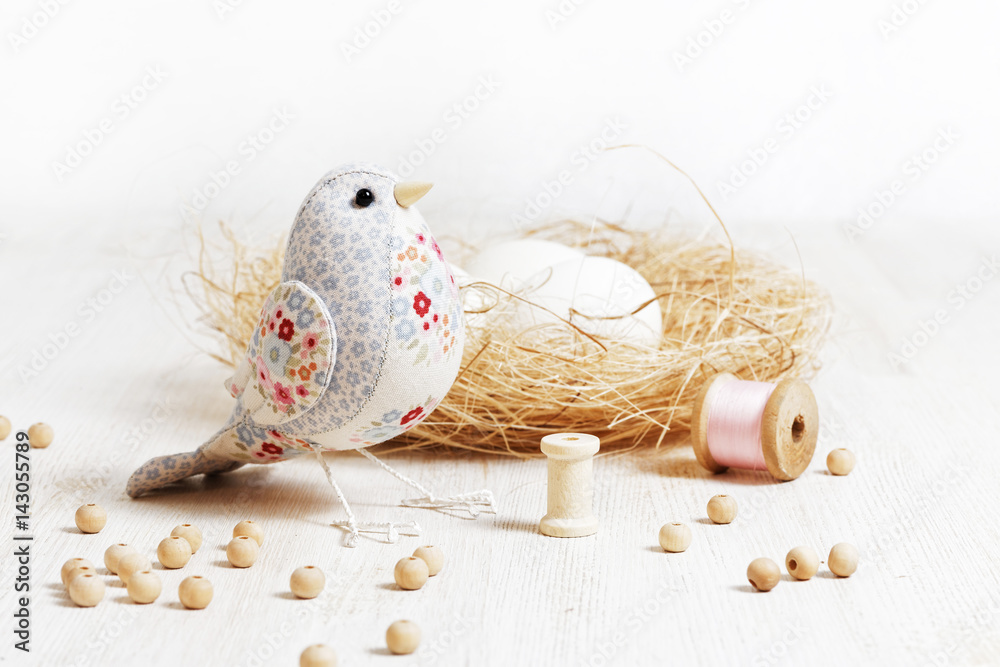 Closeup a handmade bird sewed from a cloth stands on a white wooden ...