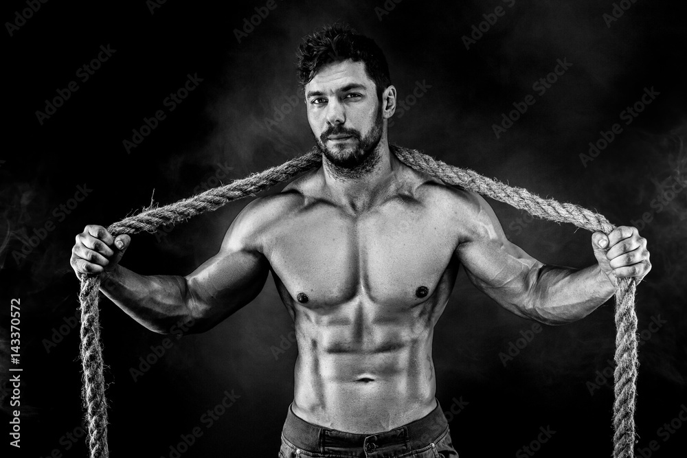 Muscular man holding rope and posing on the black background with red ...