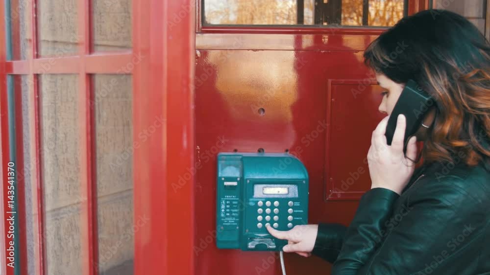 Happy girl in a red telephone booth talking on the phone in the street ...