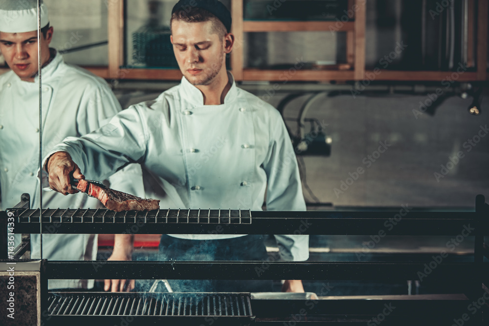 Food concept. Young handsome chef in white uniform monitors the degree ...