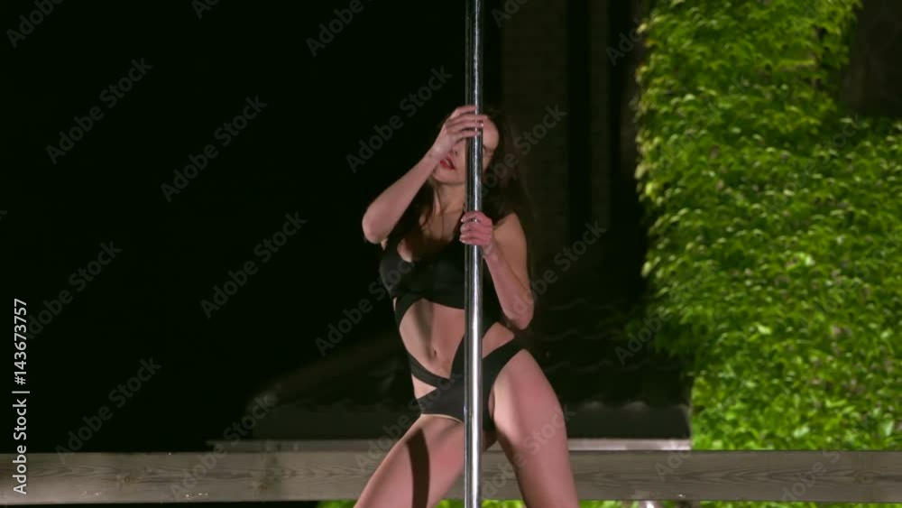 Young woman in high heels and bikini performs sensual pole dance at night in slow motion ...