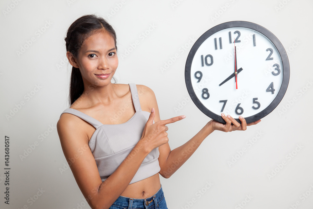 Young Asian woman point to a clock. Stock Photo | Adobe Stock