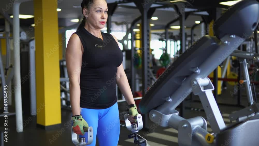 A middle-aged woman does sit-ups with a simulator in her hands. The ...