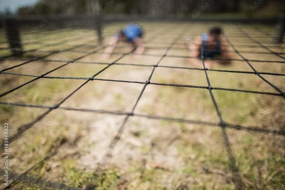 Fit man and woman crawling under the net during obstacle course Stock ...