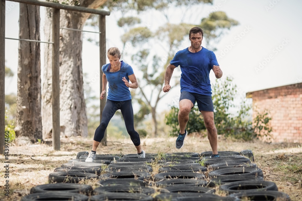 Man and woman running over the tire during obstacle course Stock Photo ...