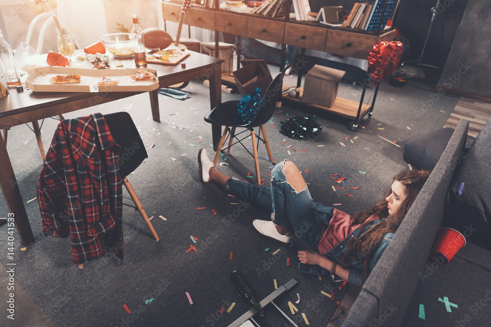 High angle view of drunk young woman lying on floor in messy room after ...