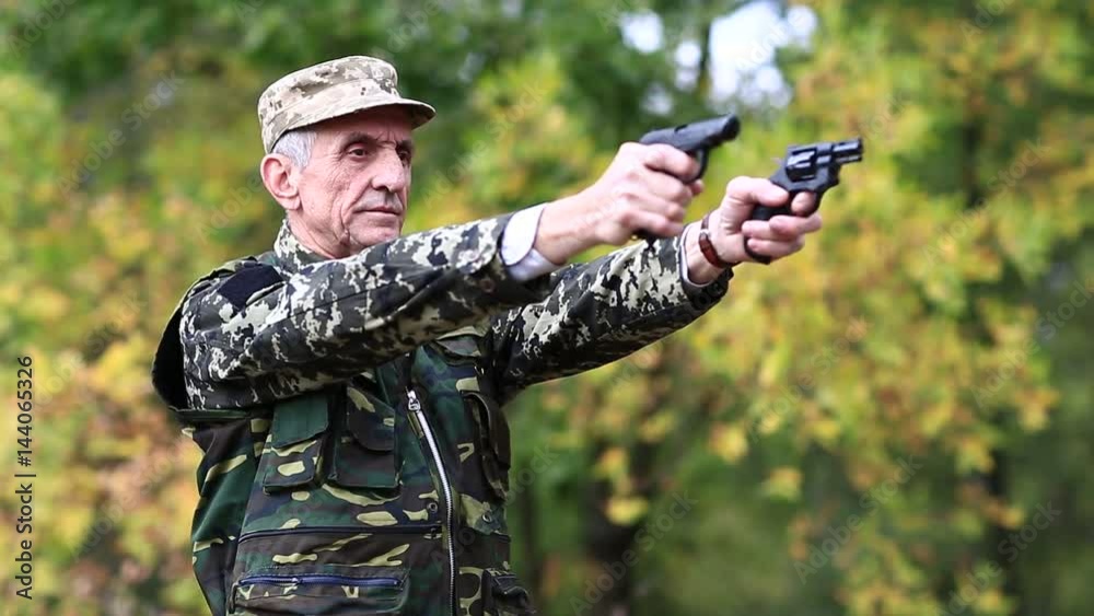 Senior man shoots a two pistols in forest. Soldier in military uniform ...