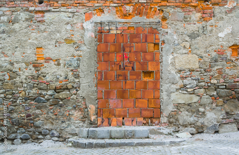 Unplastered stony wall with bricked up door. Blocked entrance to old ...