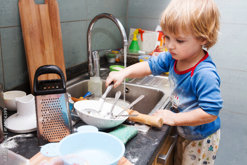 Poster A little cute boy washing dishes in the white kitchen interior ...