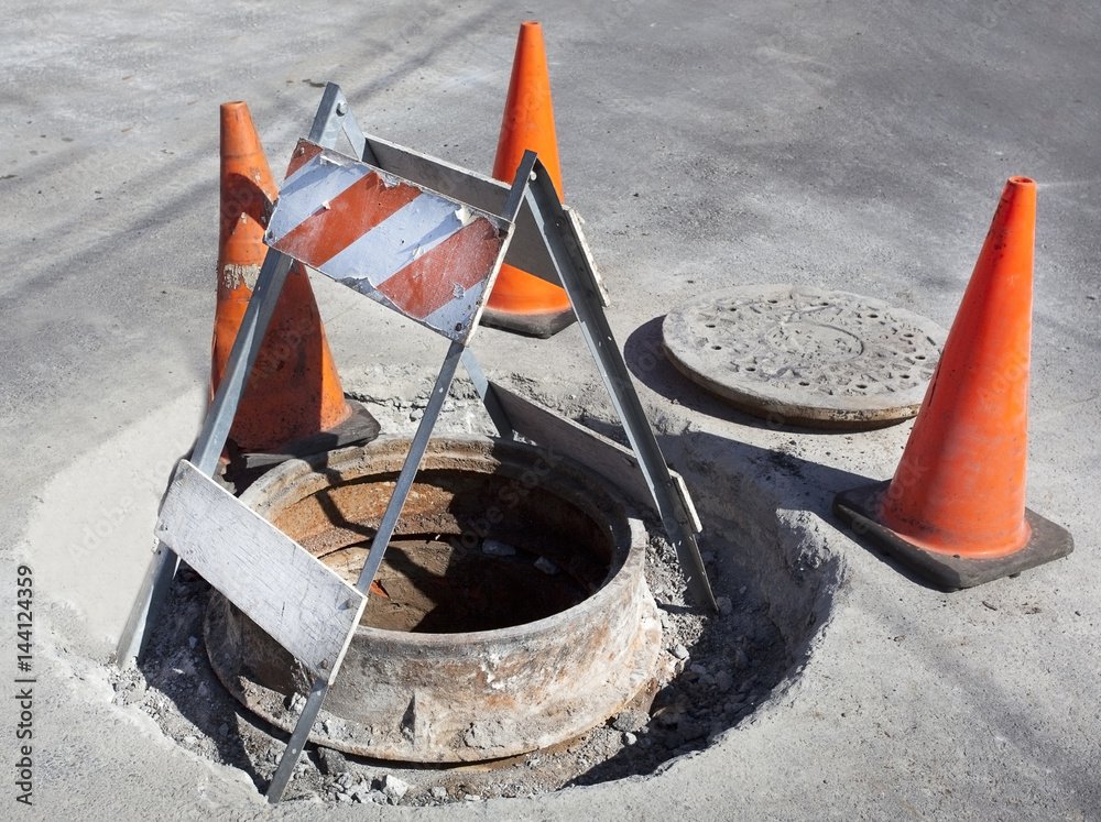 Open manhole sewer pipe with orange safety cones and wooden barricade ...