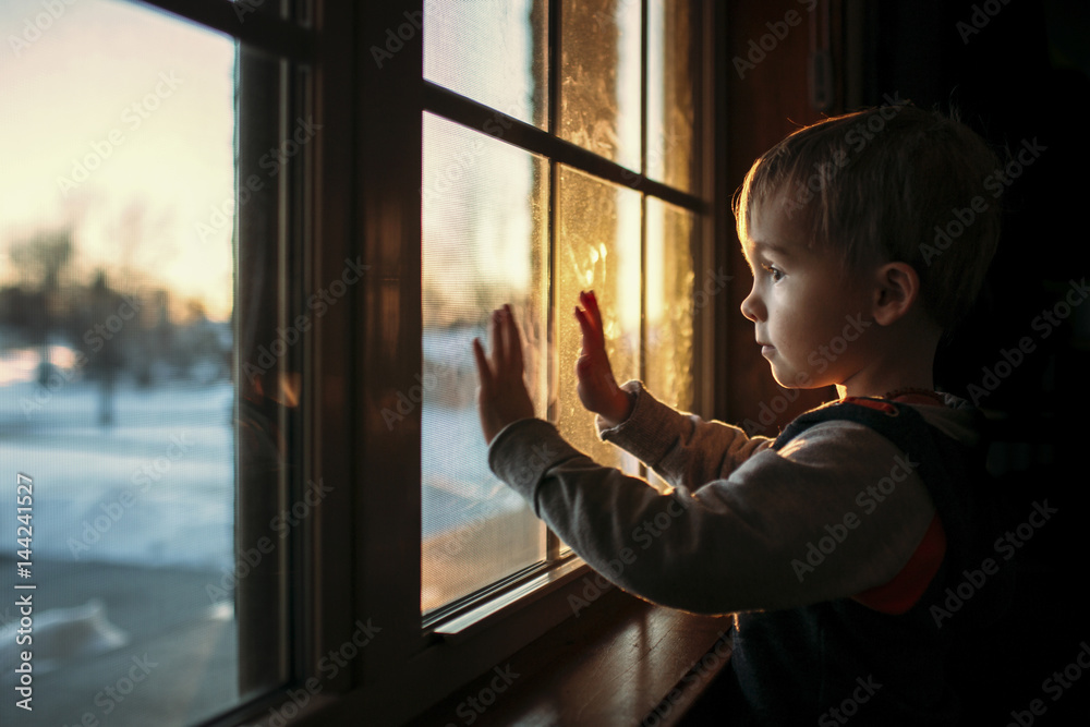Side view of boy looking through window while standing at home Stock Photo | Adobe Stock