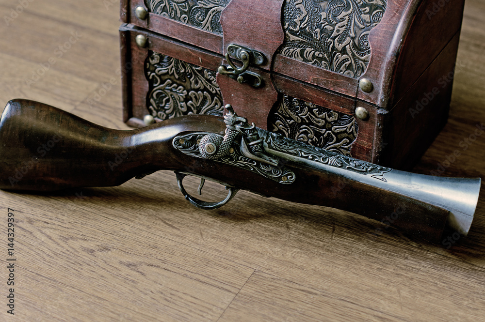 Old antique vintage pistol with a carving near an ancient wooden chest ...
