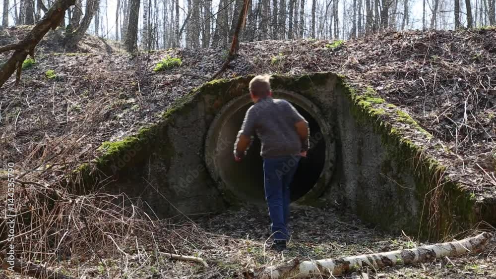 Child holding in hand flashlight walks inside of dark huge scary tube ...