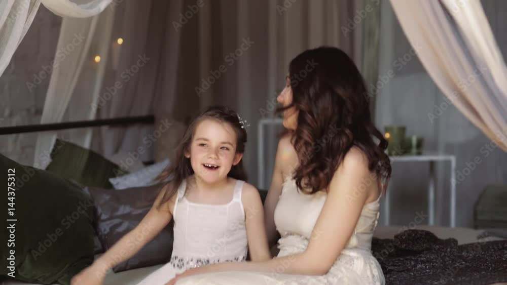 Mother and daughter hugging and cuddling in bed. Pretty little girl and ...