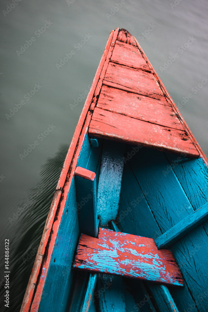 The front of a colourful wooden canoe cuts through the still water of ...