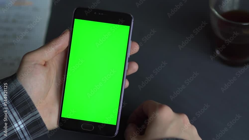 Swipe left. Man holding a smartphone in the hands of a green screen ...