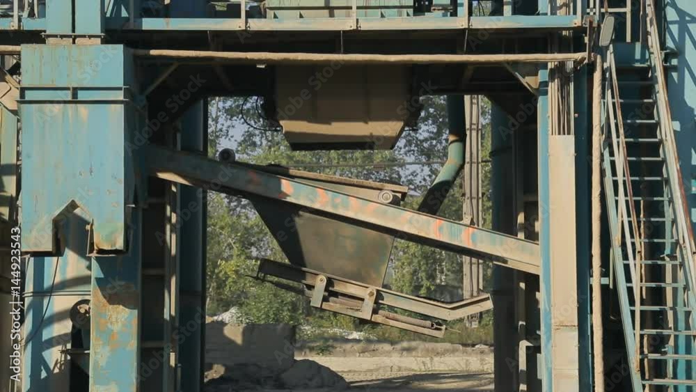 At the asphalt plant, an iron trolley approaches the storage bunker. In ...