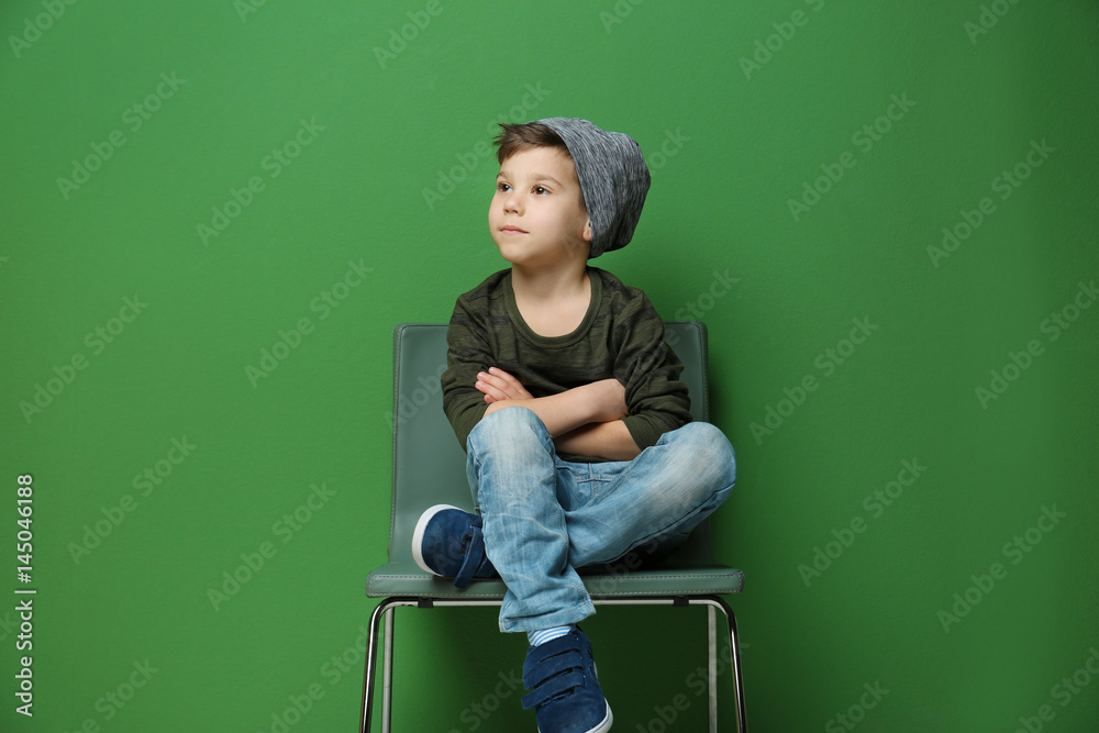 Cute stylish boy sitting on chair near color wall Stock Photo | Adobe Stock