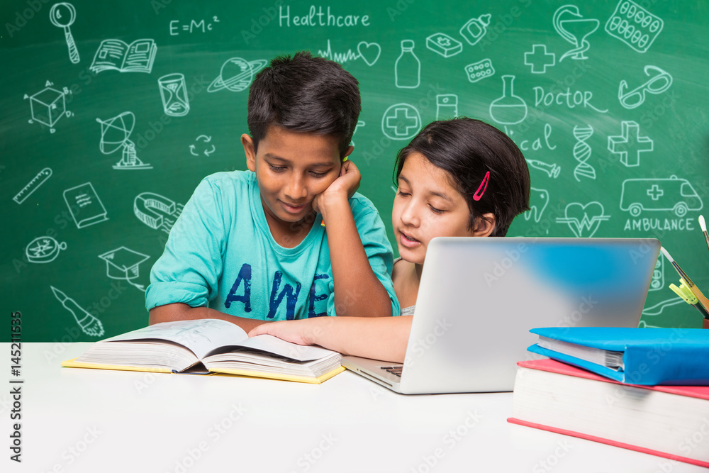 indian school kids using laptop in a classroom over green chalkboard ...